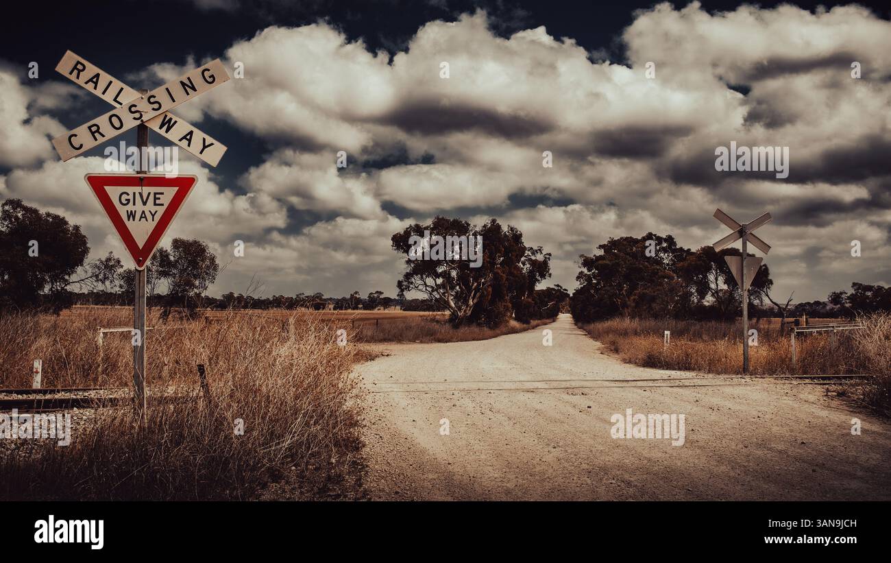A dirt road featuring a railroad crossing sign alongside a road sign ...