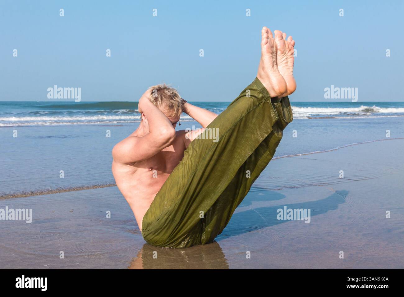 Young man doing sit ups during fitness training on sea beach Stock ...