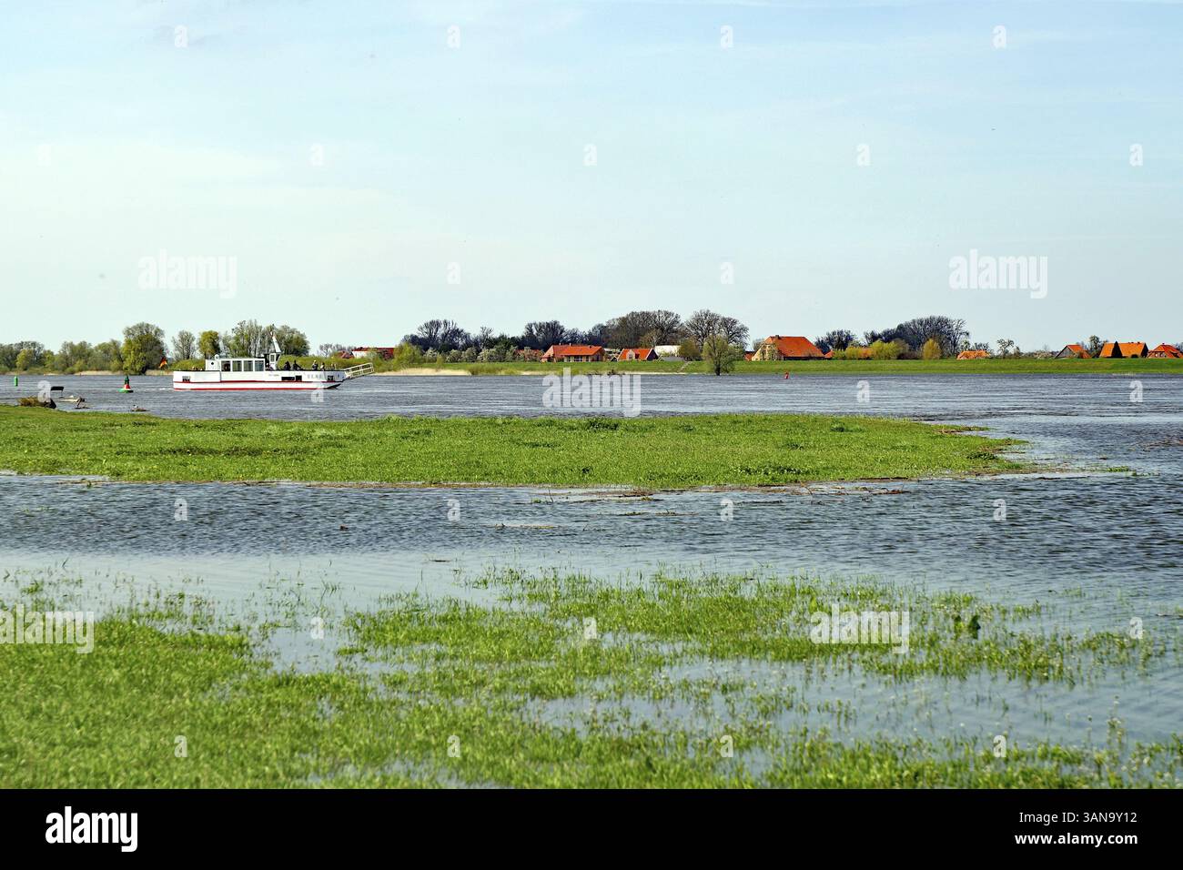 Wide river with boat and wide view of green fields and a small village ...