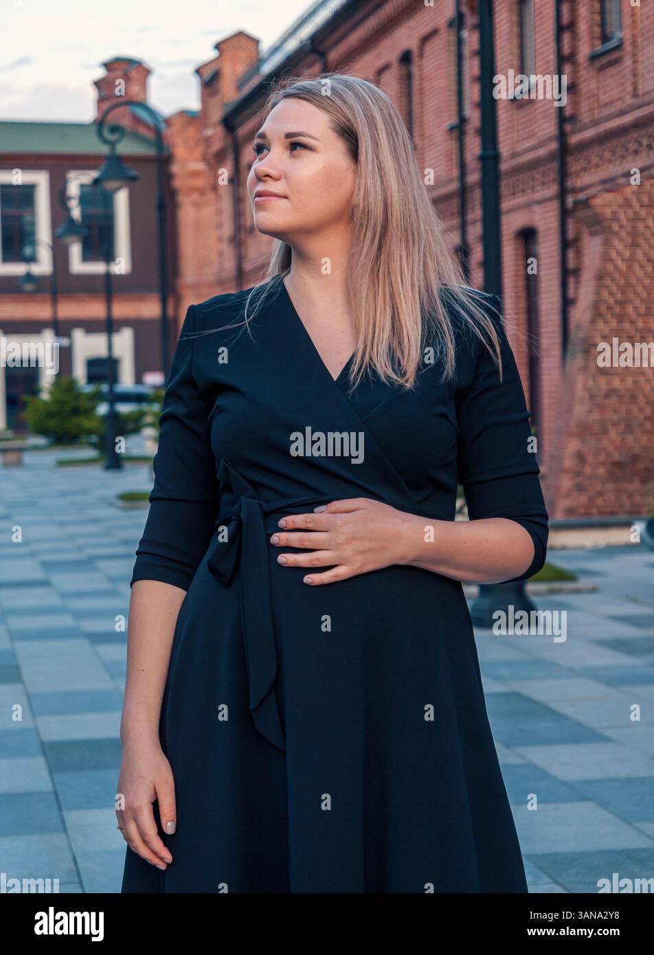 Young pregnant woman in a black dress poses confidently outside ...