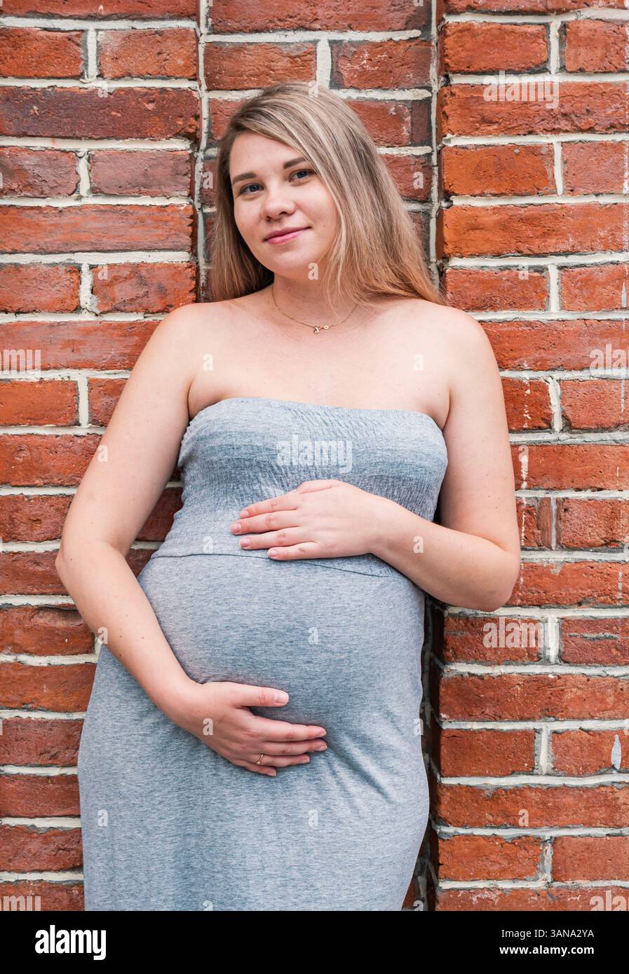 Young pregnant woman stands confidently, cradling her baby bump while ...