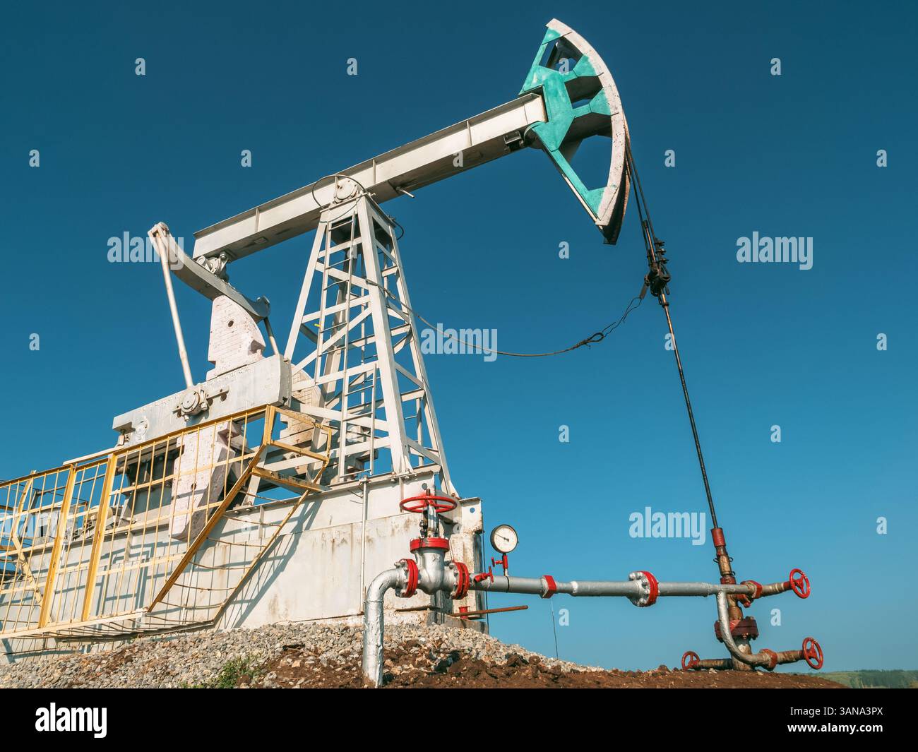 A large oil pump jack operates in an open field, extracting crude oil ...