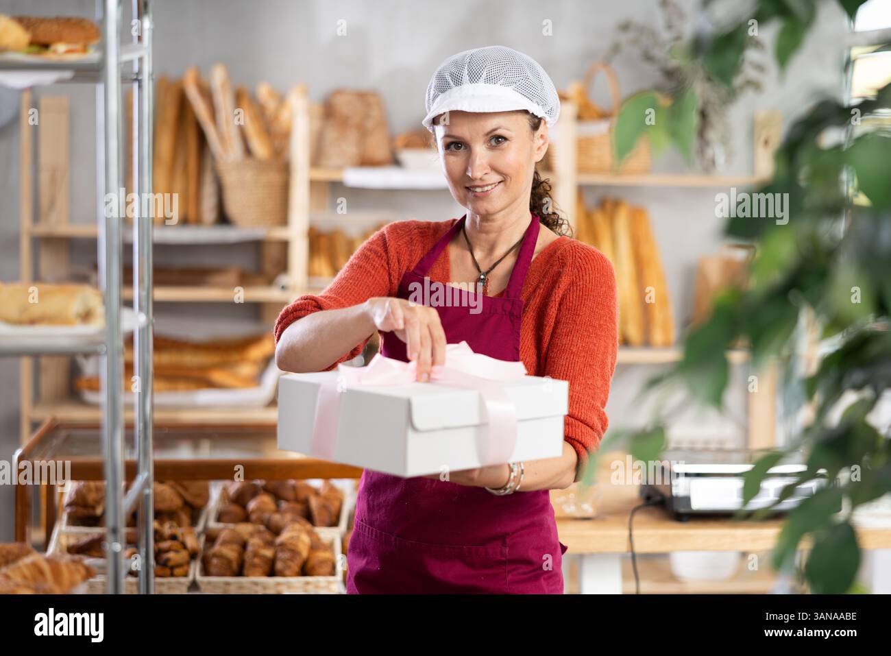 Woman entrepreneur owner of bakery holds out paper bag with pastries in ...