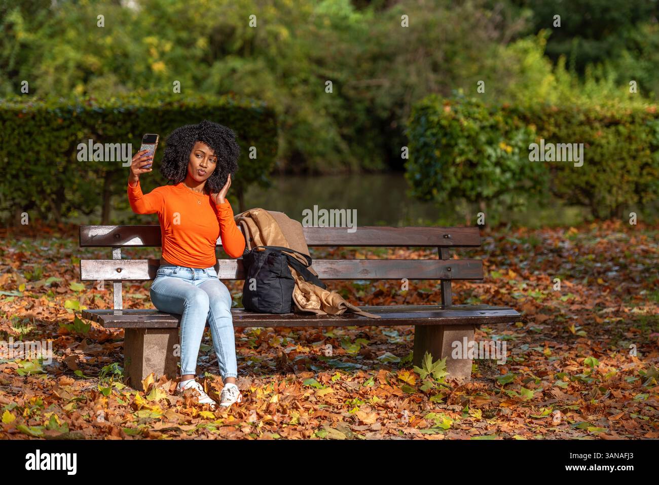 Beautiful Gen Z taking selfies while sitting on a park bench in autumn ...
