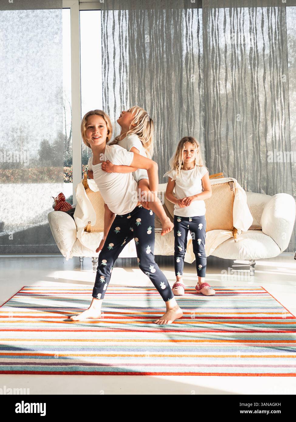 Three sisters are playing together in a bright living room. One child ...