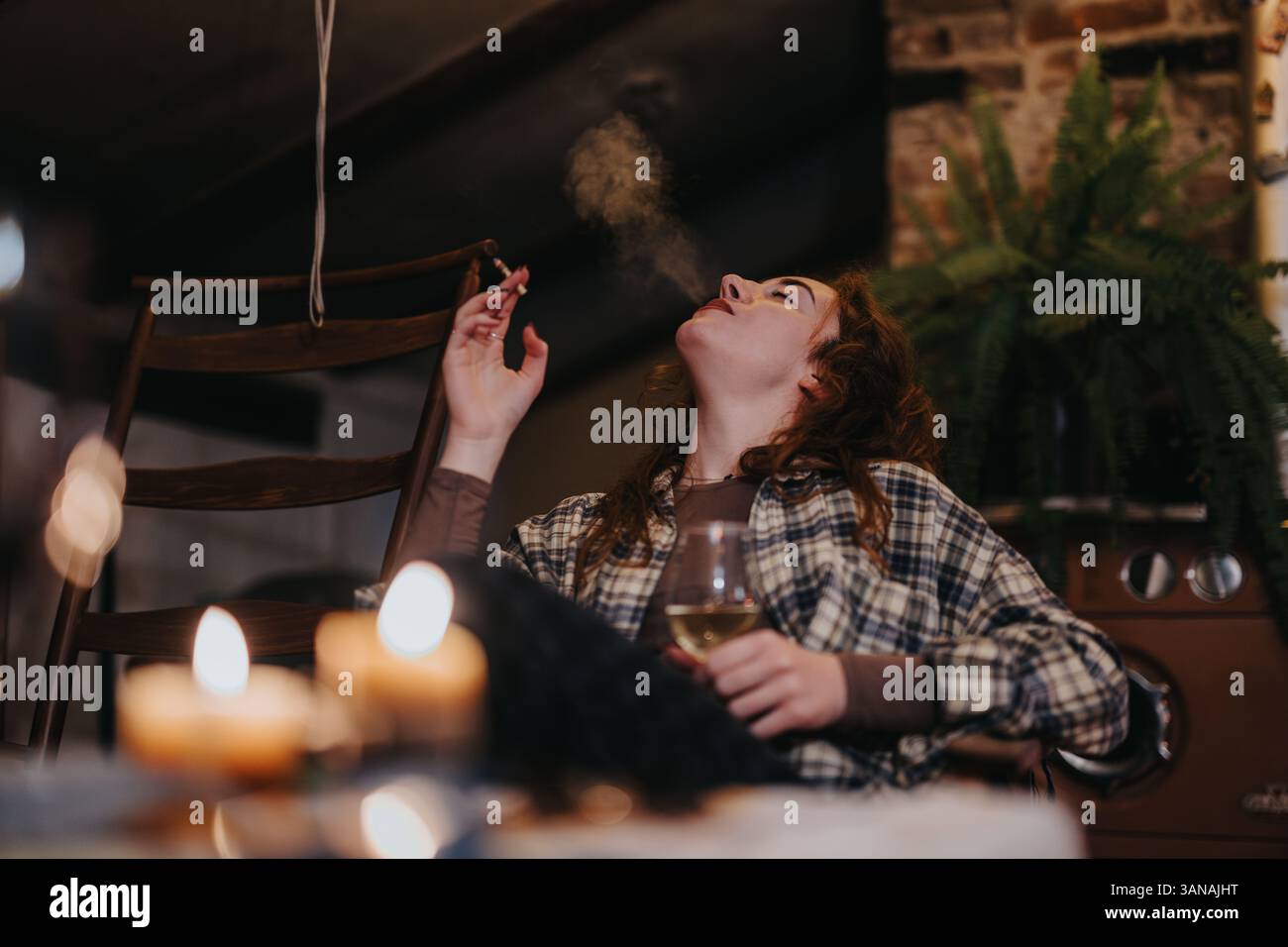 Relaxed woman smoking and drinking wine around a cozy indoor setting ...