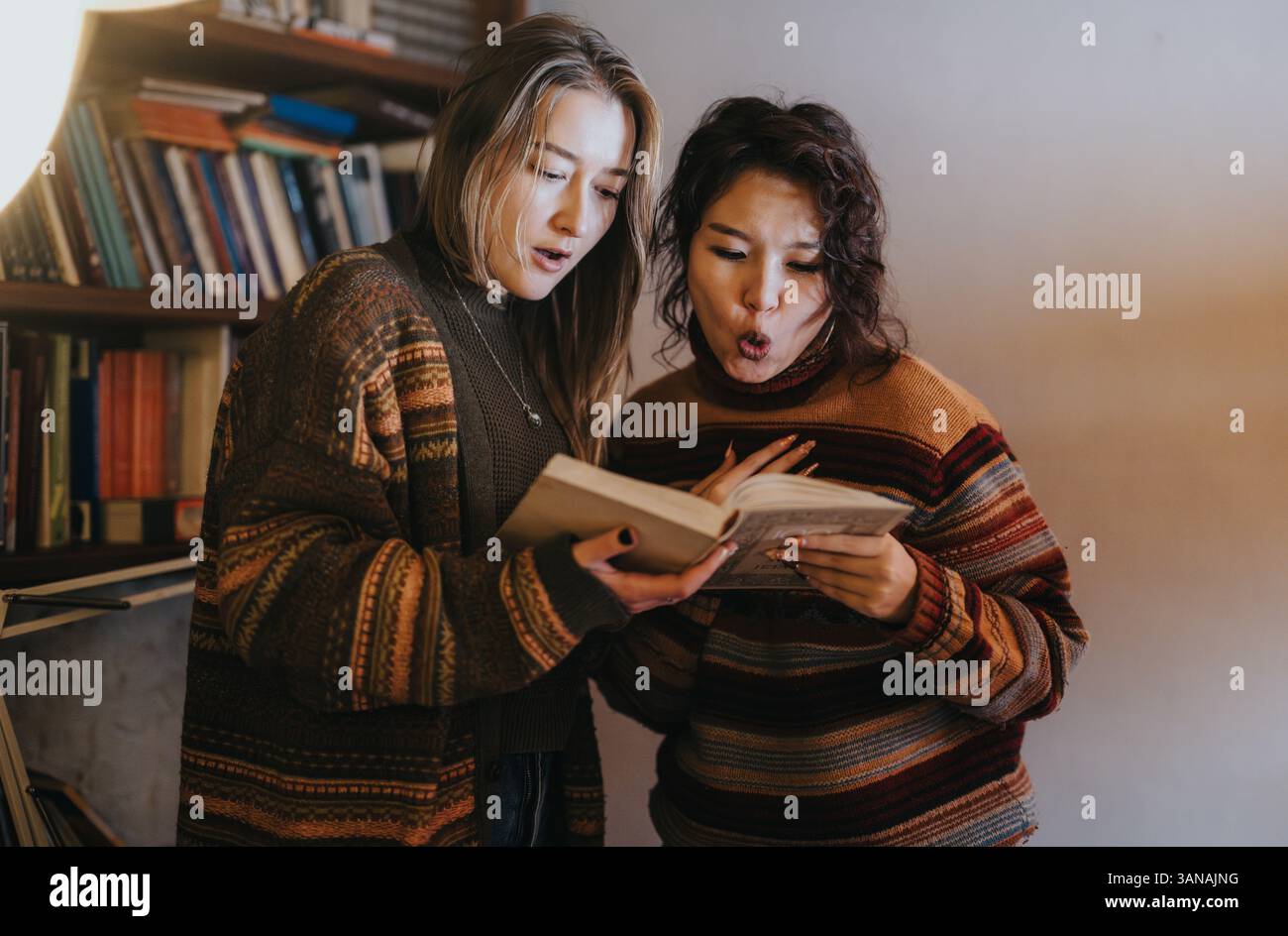 Two friends sharing a surprising moment while reading a book together ...