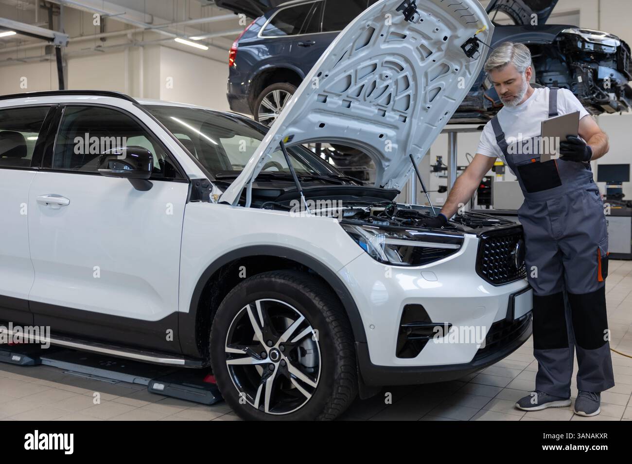 Auto mechanic in workshop holding tablet performing diagnostic check on ...