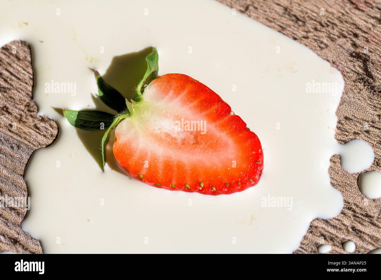 Half a strawberry (Fragaria × ananassa) in cream on rustic wood ...