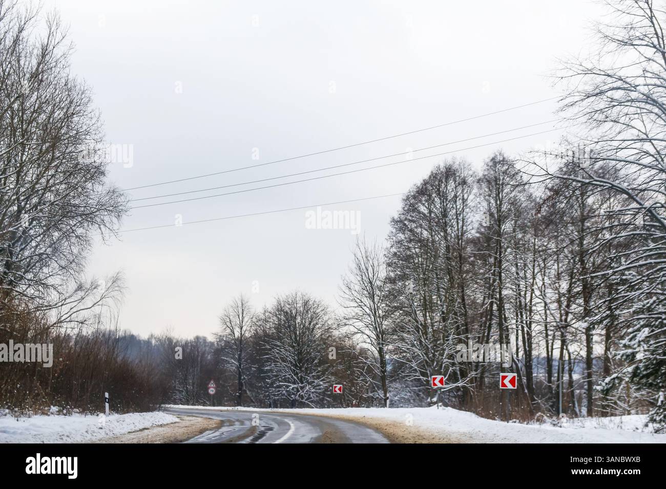 Snow-covered winter road with visible traffic signs warning of slippery ...