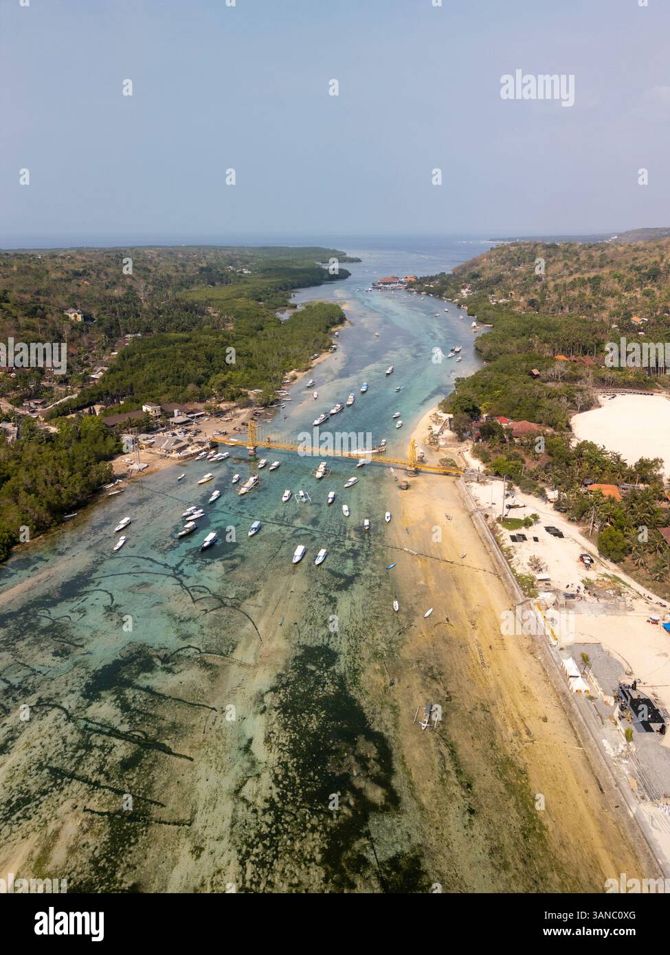 Aerial view of yellow bridge over clear water with boats and lush ...