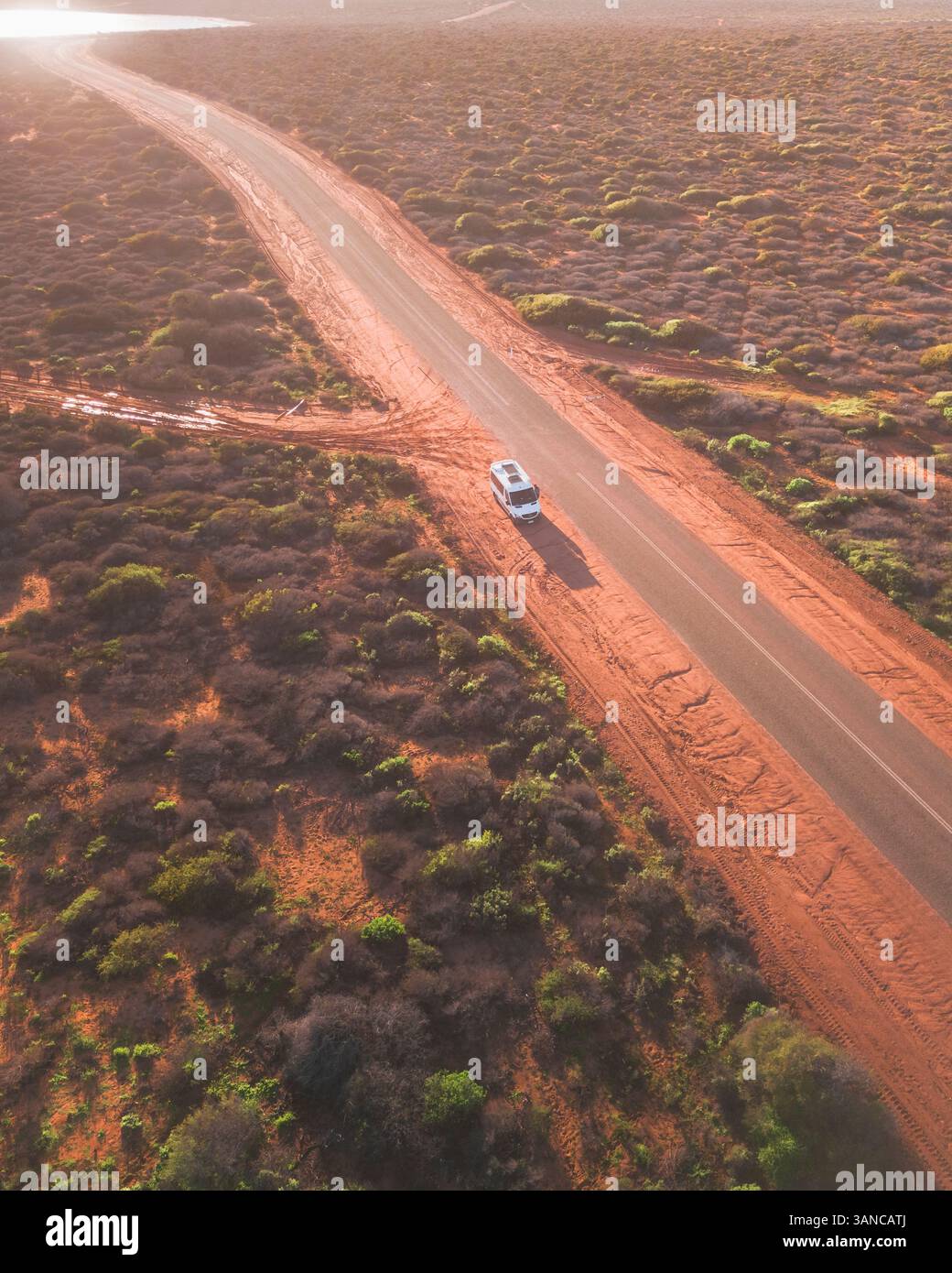 Aerial view of a dusty road winding through a vast and arid desert landscape at sunset, Denham ...