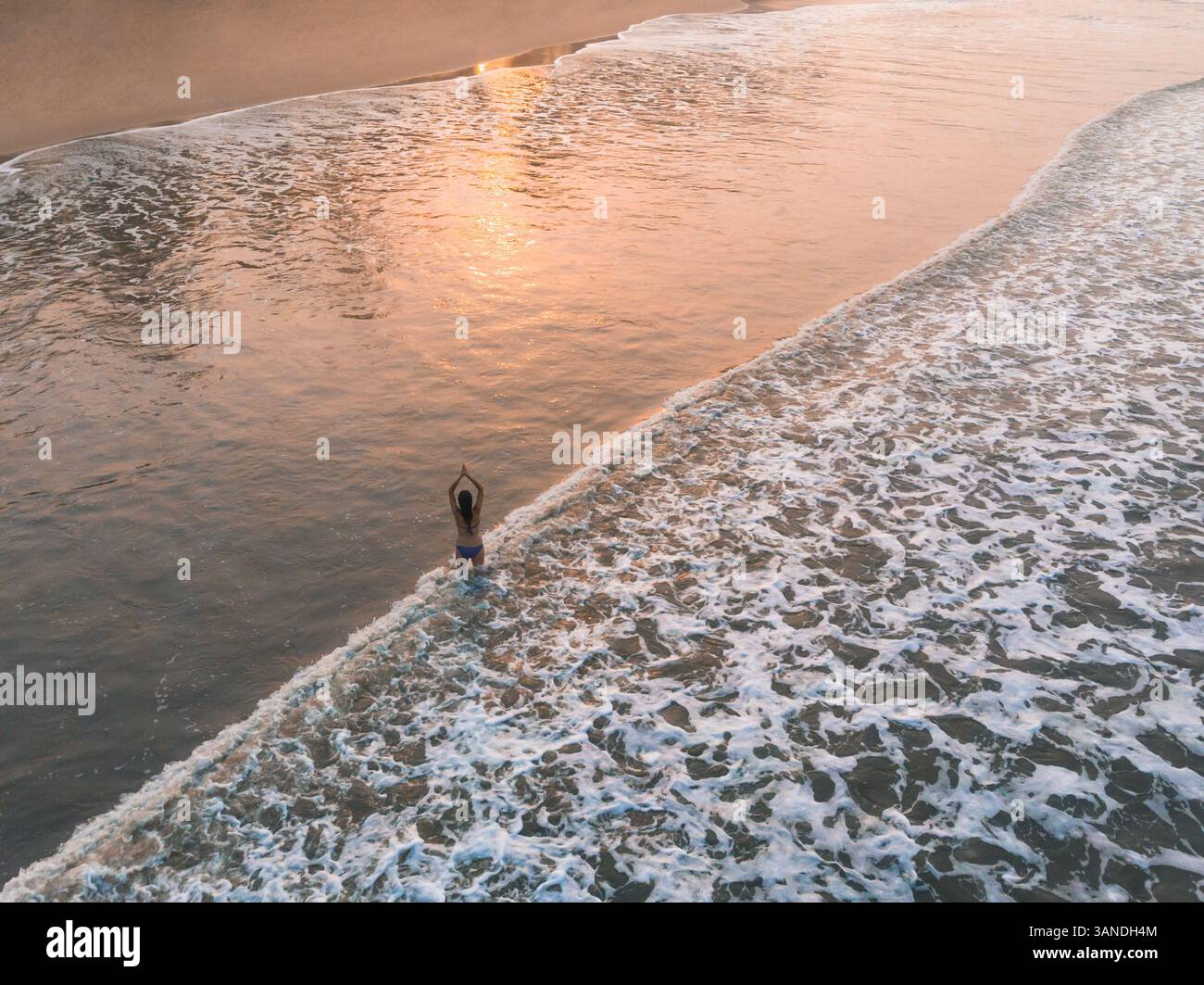 Aerial view of a woman doing yoga in the ocean during sunrise on ...