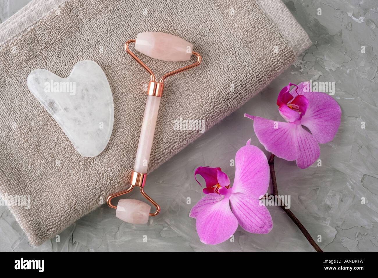 Rose quartz face roller and gua sha stone on towel with pink orchid on ...
