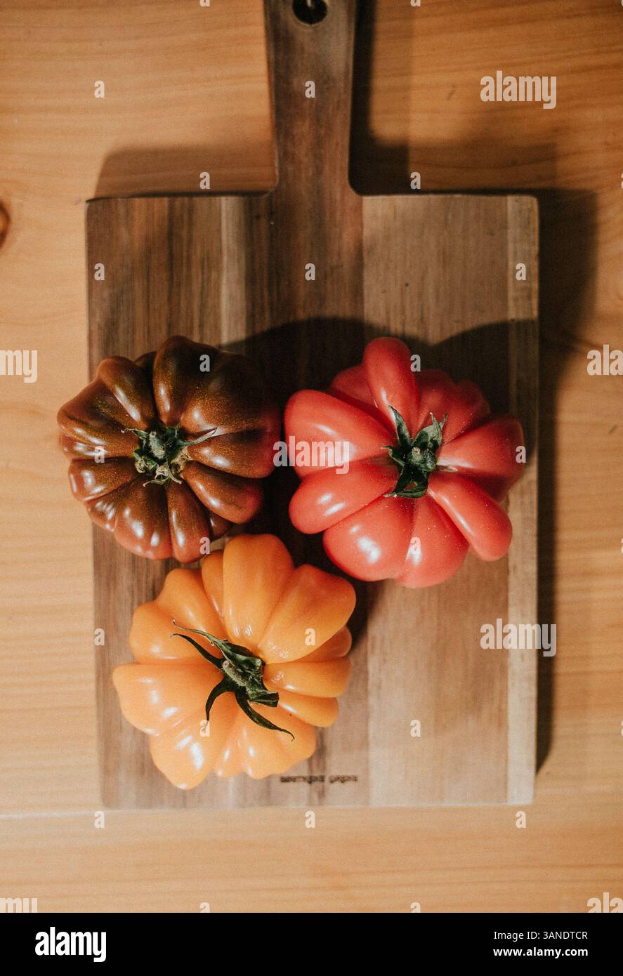 Three different colored tomatoes are on a wooden cutting board. The ...