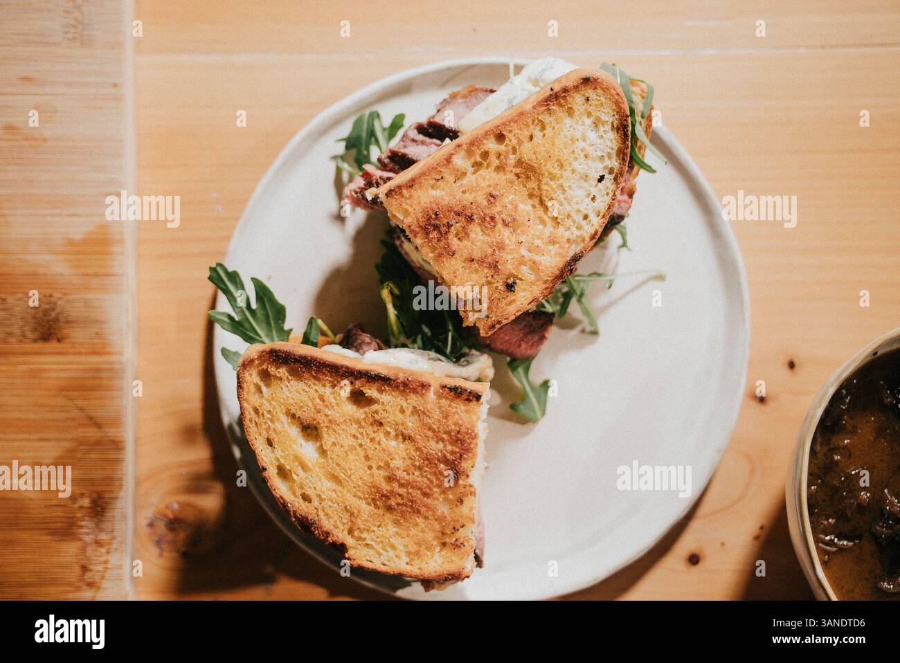 A sandwich is cut in half and placed on a white plate. The sandwich is ...