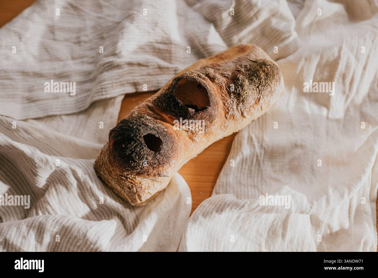 A piece of bread with burnt edges sits on a white cloth. The bread is ...