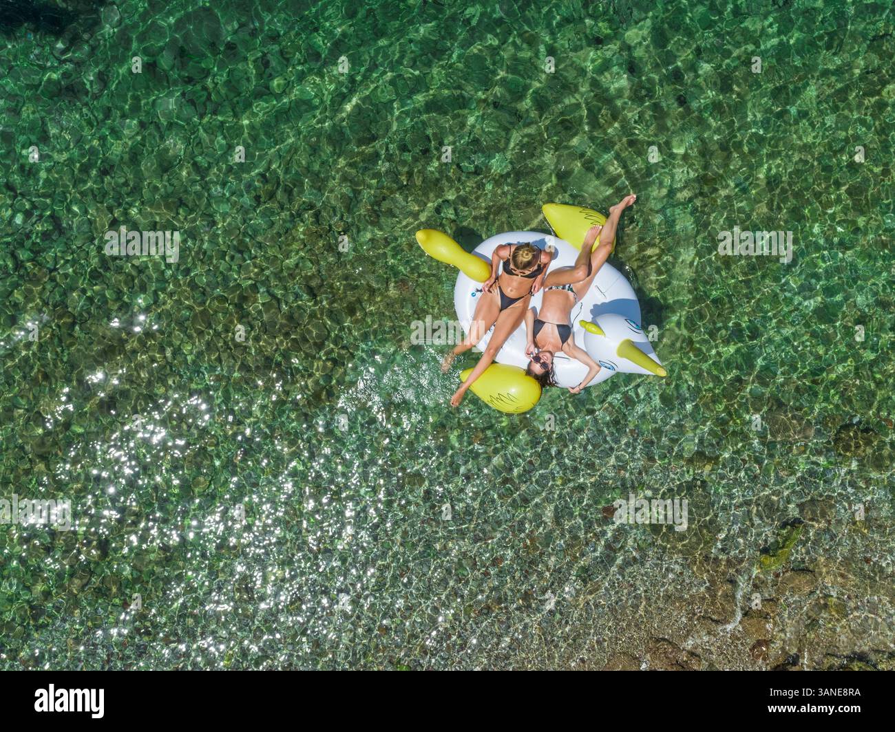 Aerial view of two women in bikinis floating on inflatable animal ...