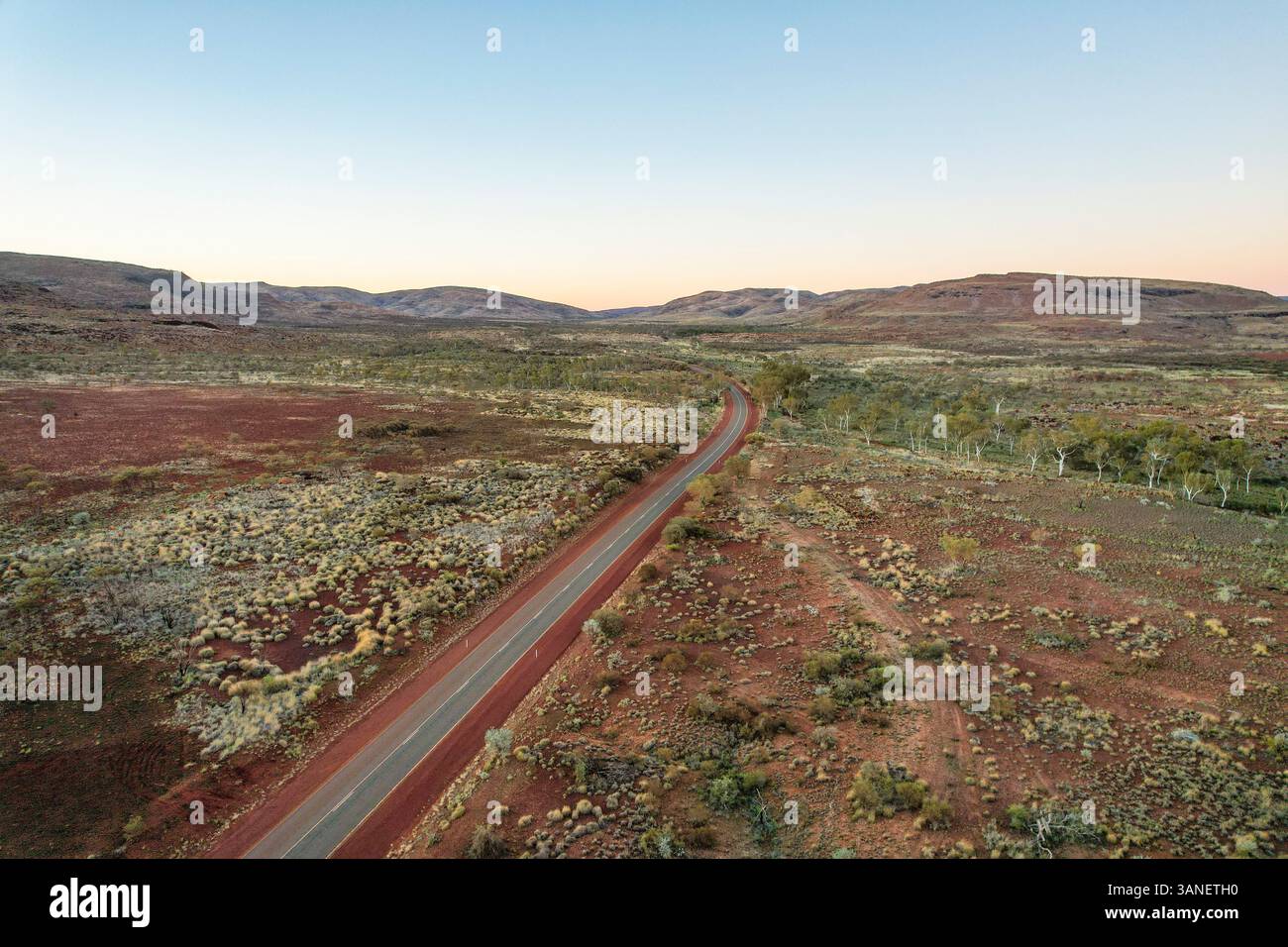 Aerial view of winding road through rugged hills and barren bushland at sunset, Karijini ...