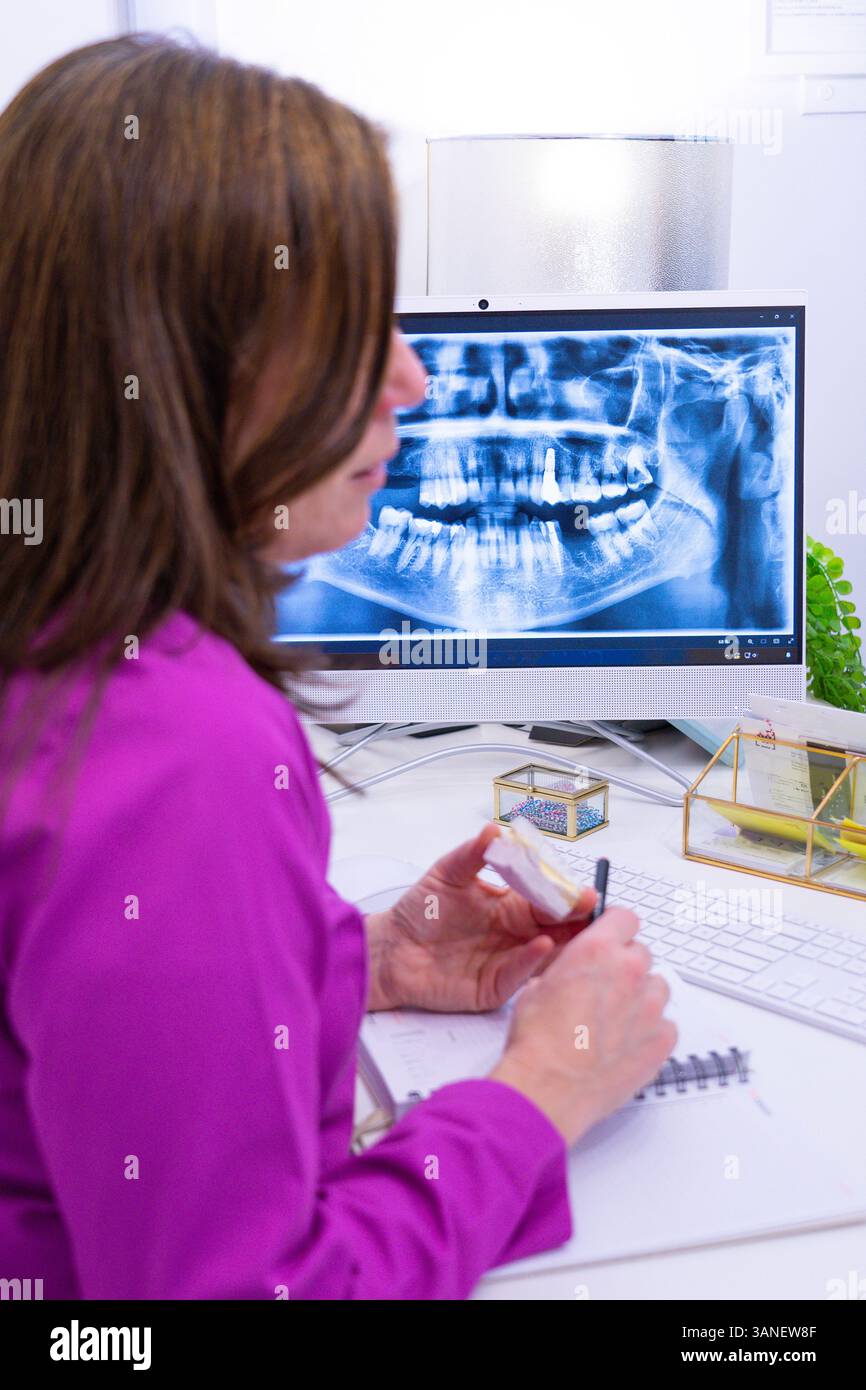 Dentist examining a dental x-ray on a computer monitor while holding a ...