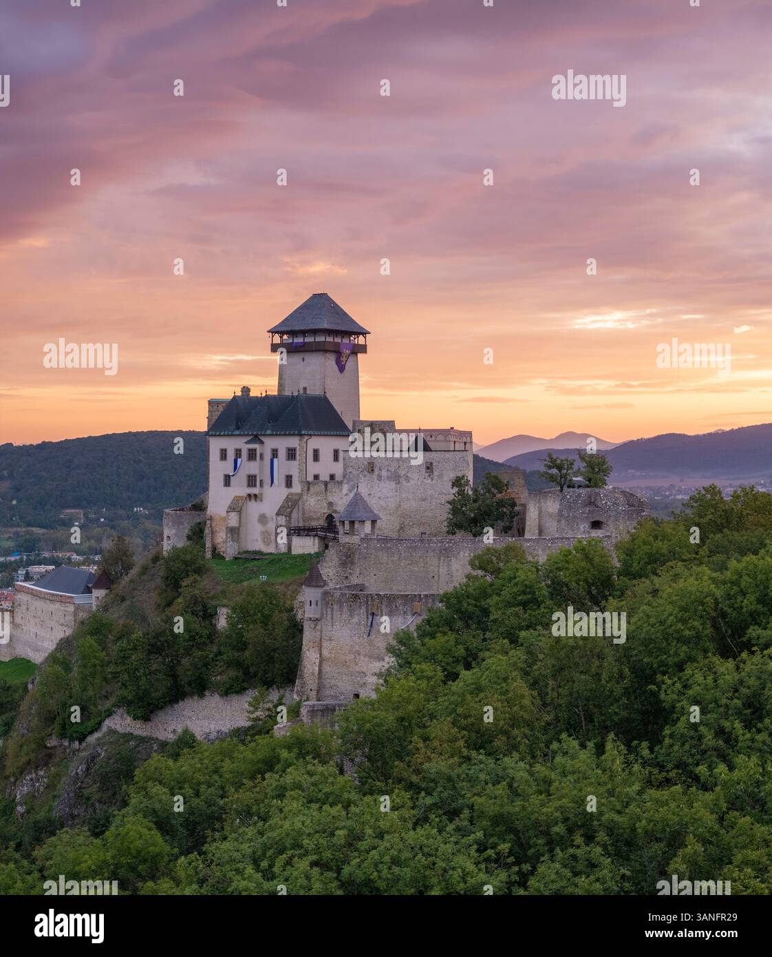 Aerial view of Trencin Castle at sunrise surrounded by trees and clouds ...