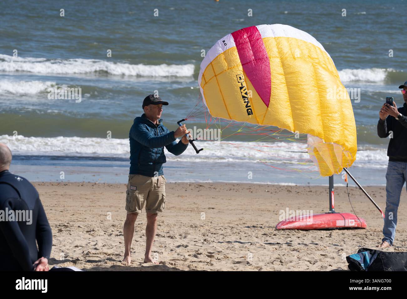 A man practices flying a hydrofoil parawing on a beach with the sea ...