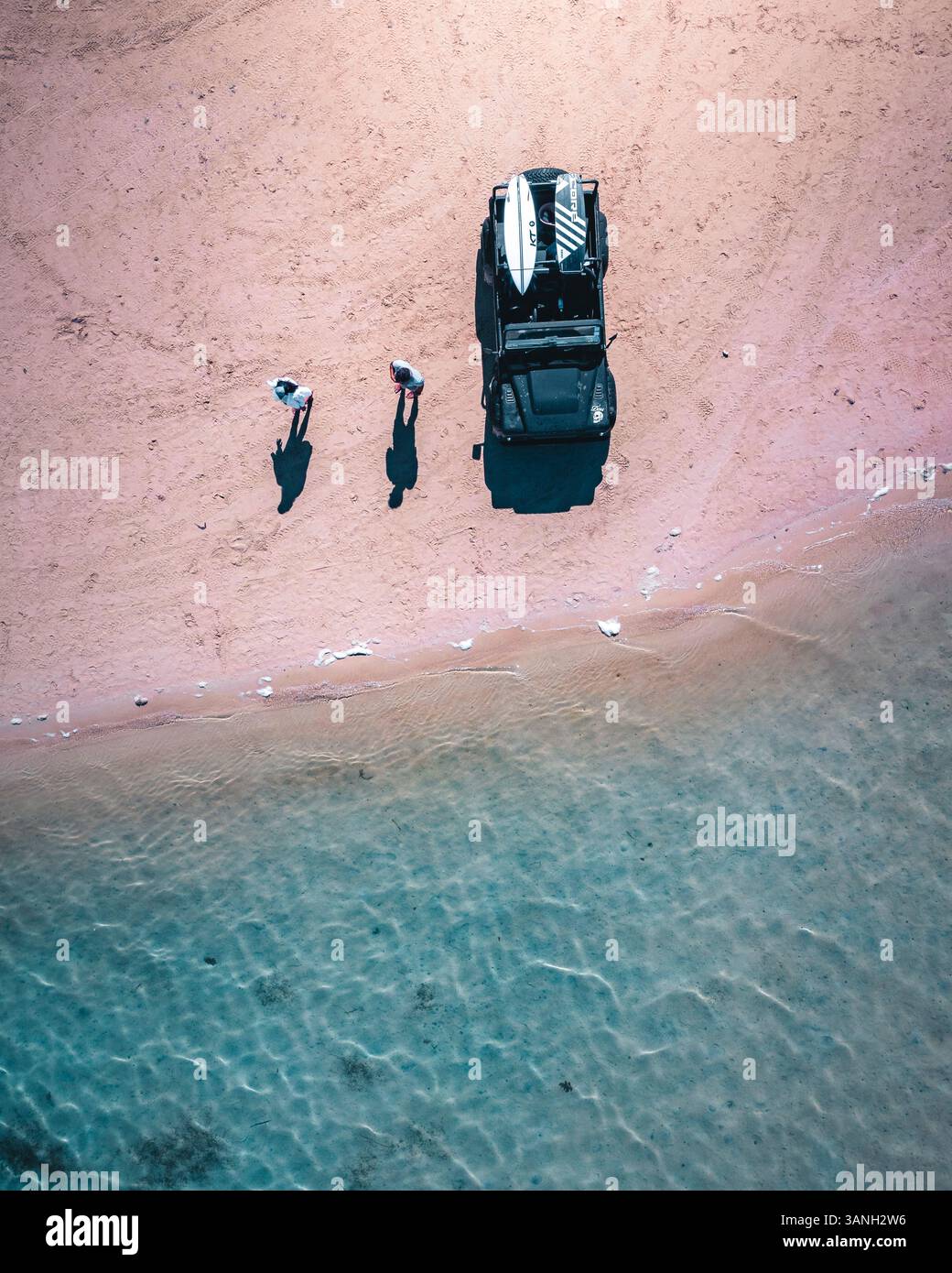 Aerial view of an off road car parked along the shoreline on the beach ...