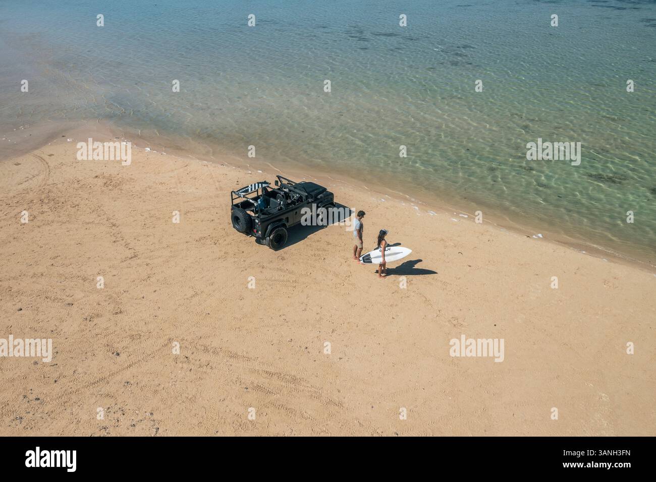 Aerial view of an off road car parked along the shoreline on the beach ...