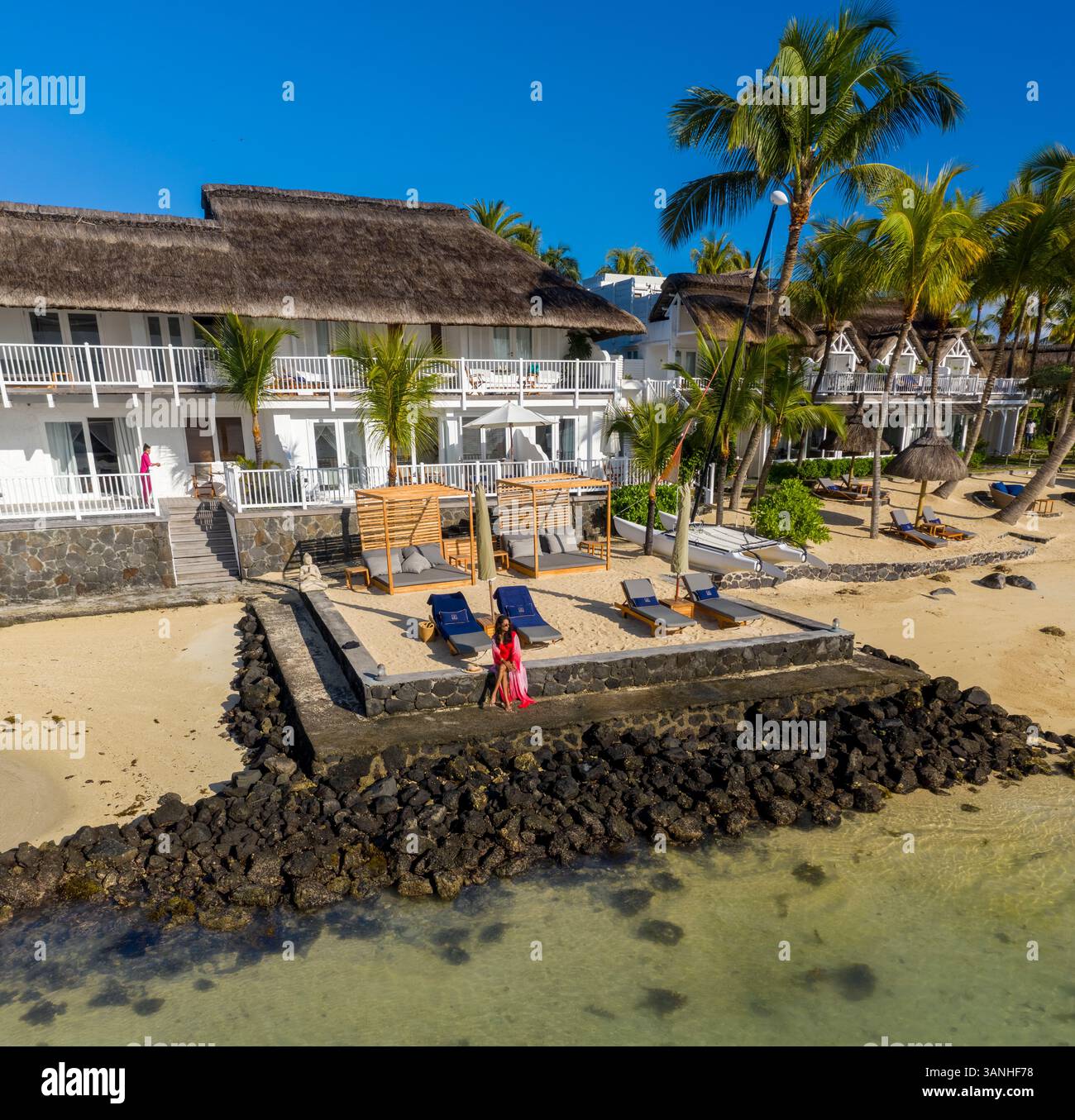 Aerial view of a woman relaxing on a beach bed in a luxury resort along ...