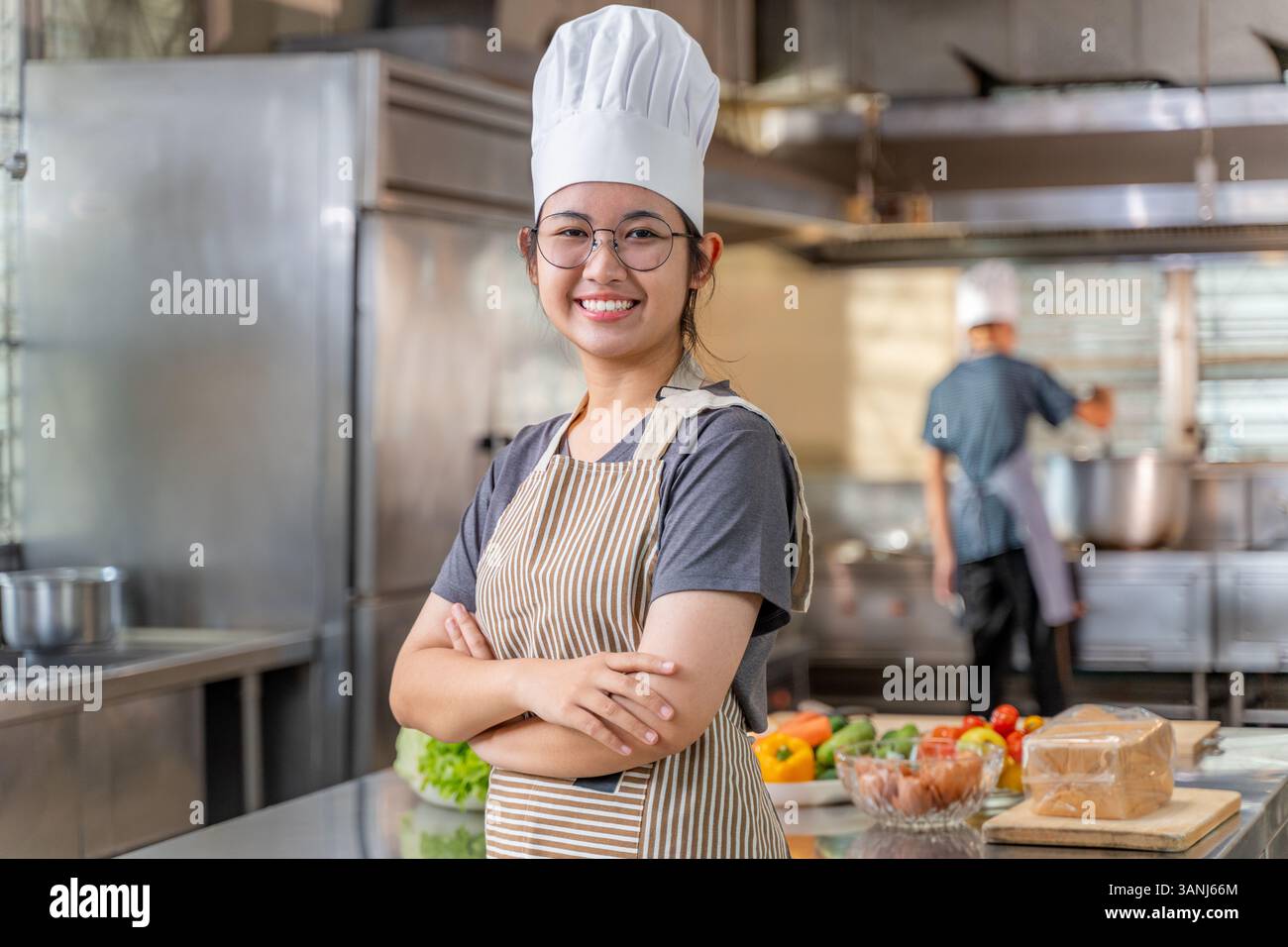 Confident young female chef smiling and standing with arms crossed in a ...