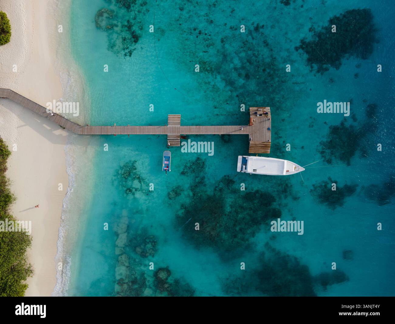 Aerial view of boat at end of pier and boardwalk on crystal clear blue ...