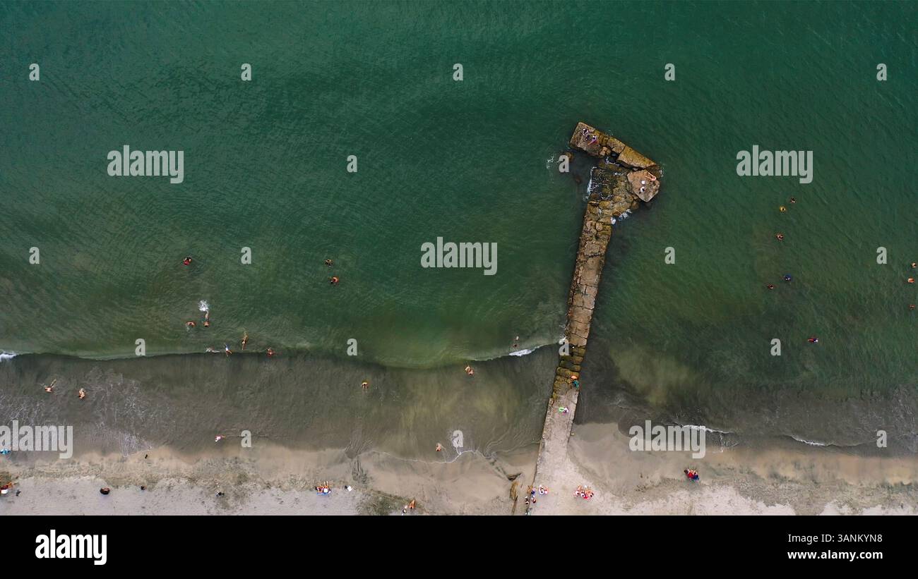 Aerial view of beach with pier, ocean waves, and people enjoying the ...