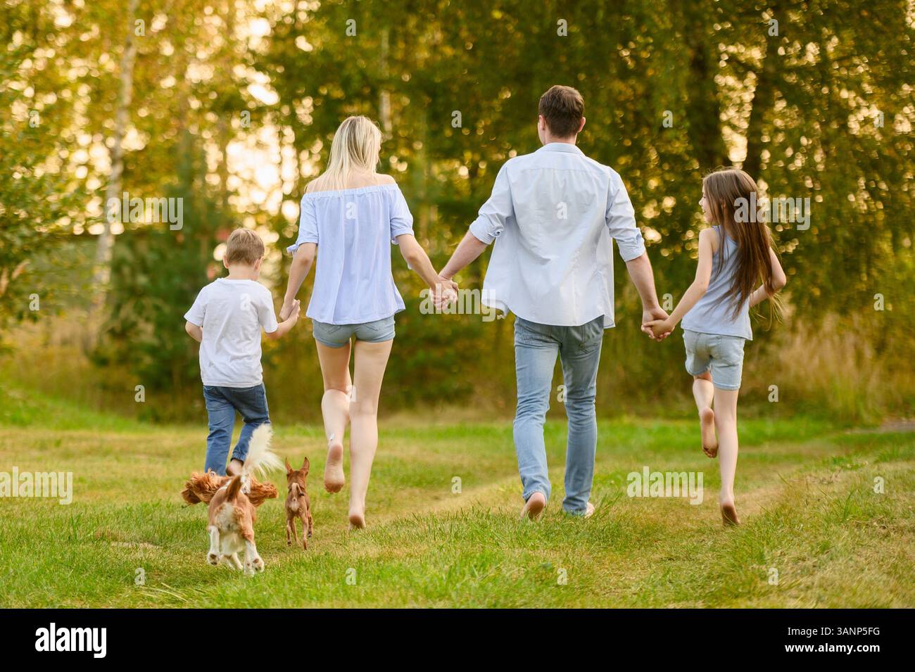 Family running barefoot holding hands on grass, view from behind ...