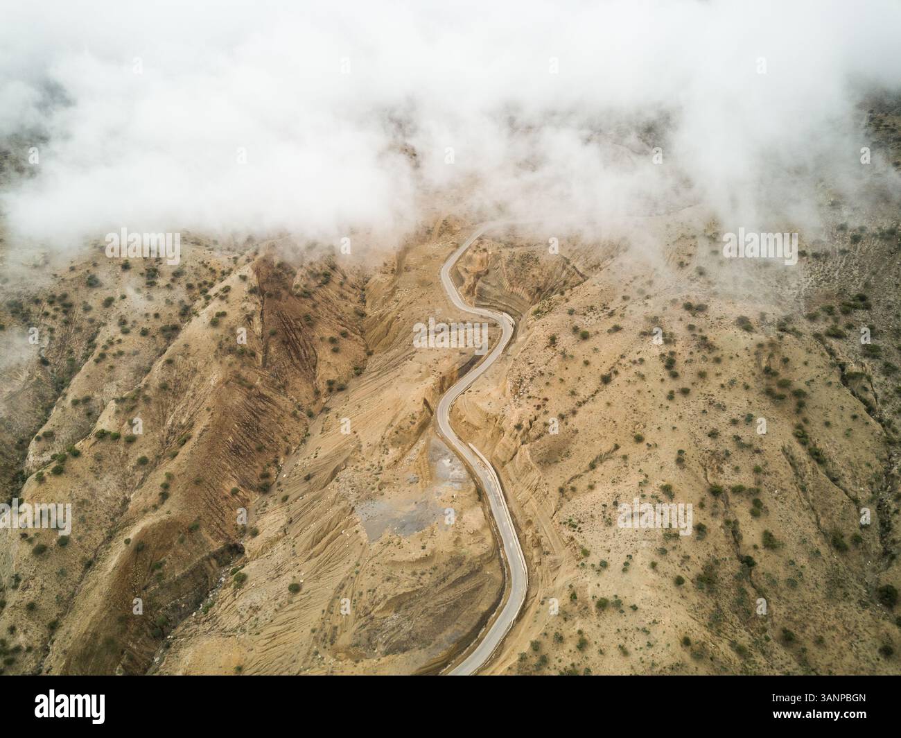 Aerial view of clouds falling on a serpentine empty road in the ...