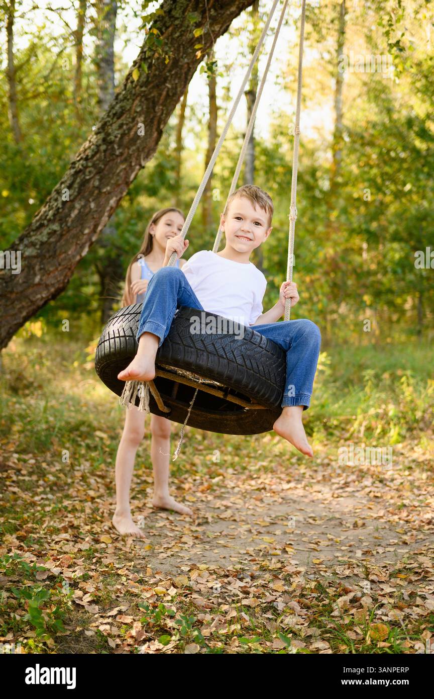 Boy and girl enjoying time and play together. Sister swinging brother sitting comfortably on ...