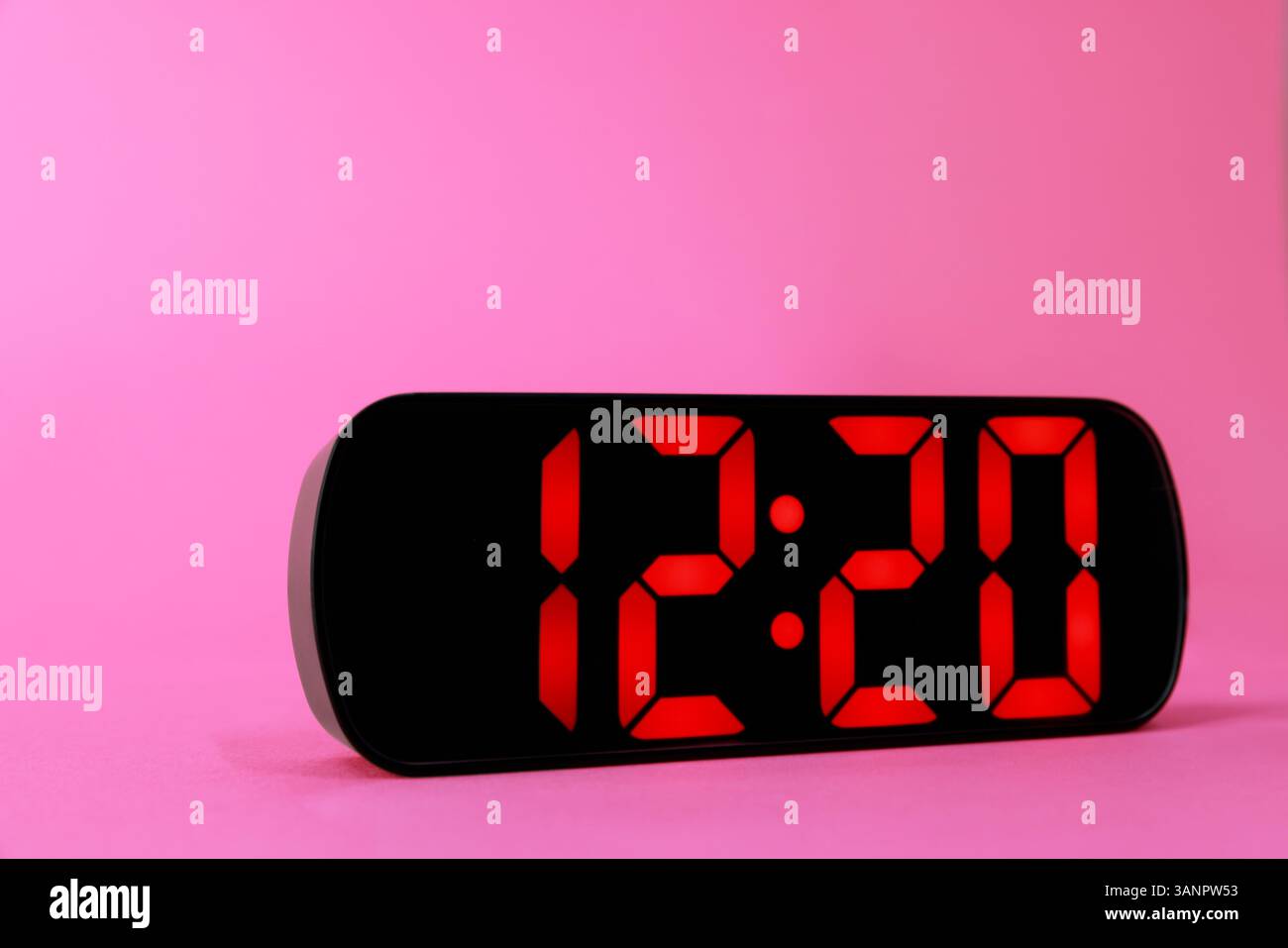 Digital alarm clock showing 12:20 o'clock on pink background, closeup ...
