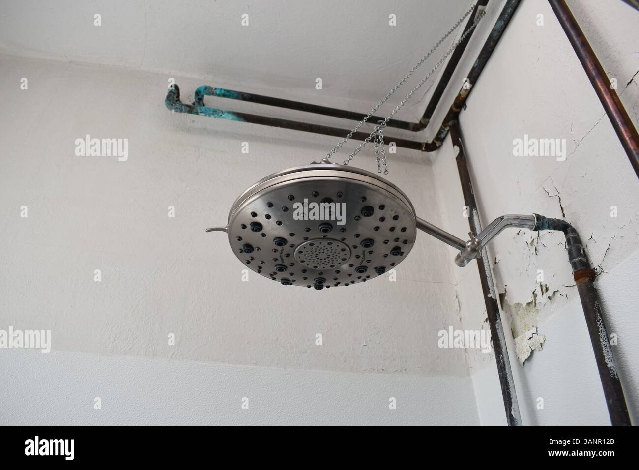 A classic, aged shower head on an old, peeling wall with exposed ...