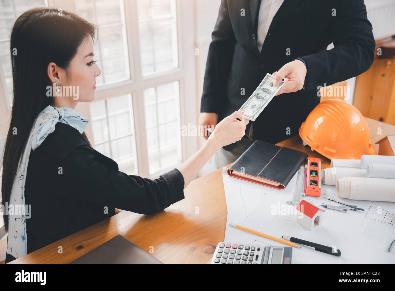 Man offering batch of hundred dollar bills to female architect ...