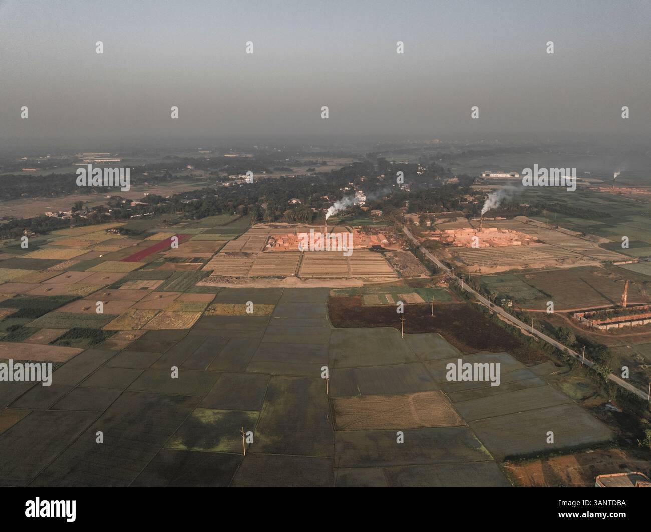 Aerial view of brick fields and factory with smoke plumes over green ...