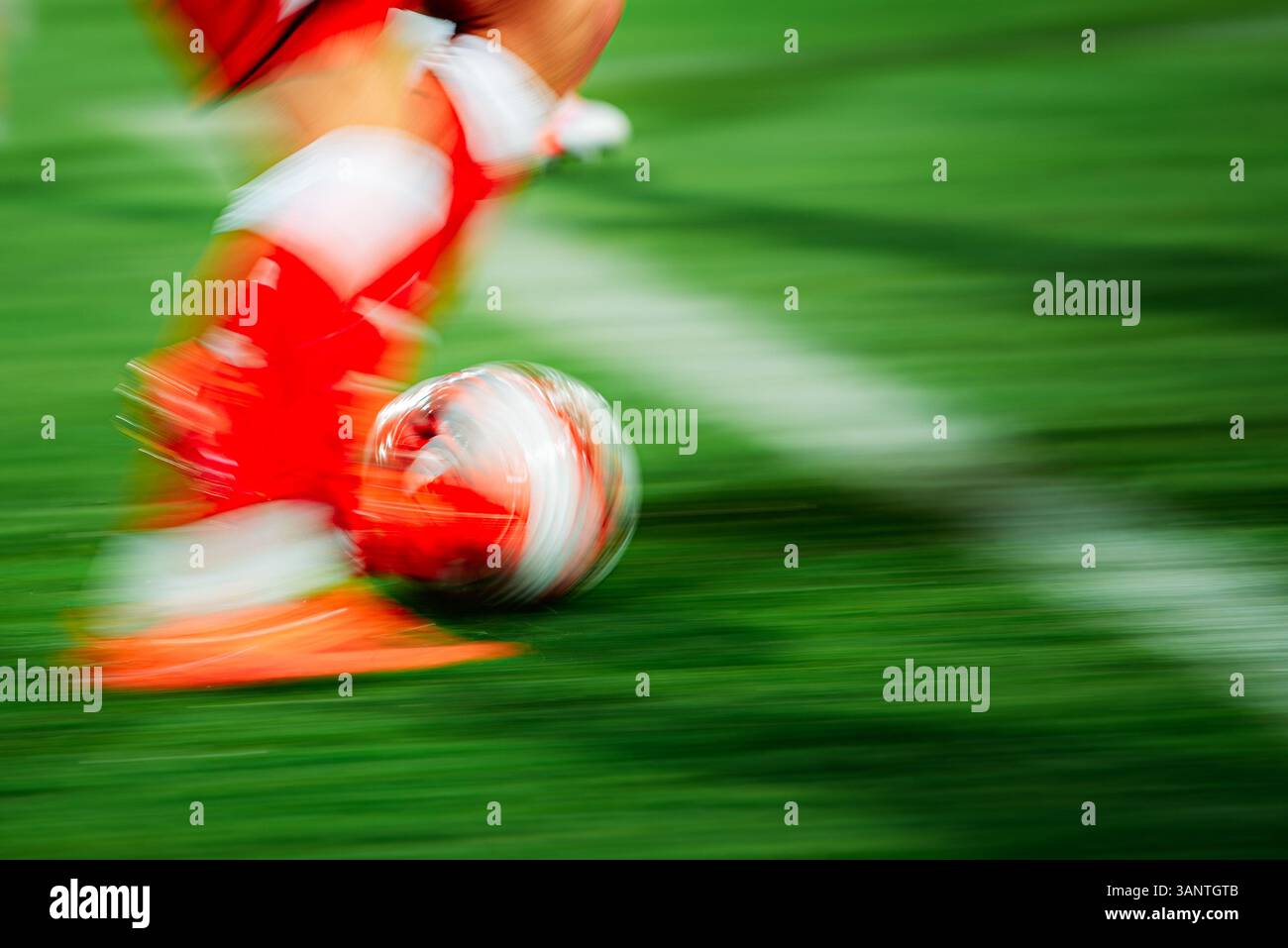 Dynamic motion blur of a soccer player in red kicking a white-red ball ...