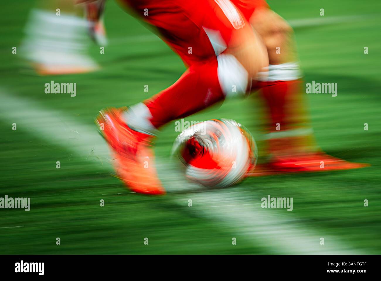 Dynamic motion blur of a soccer player in red kicking a white-red ball ...