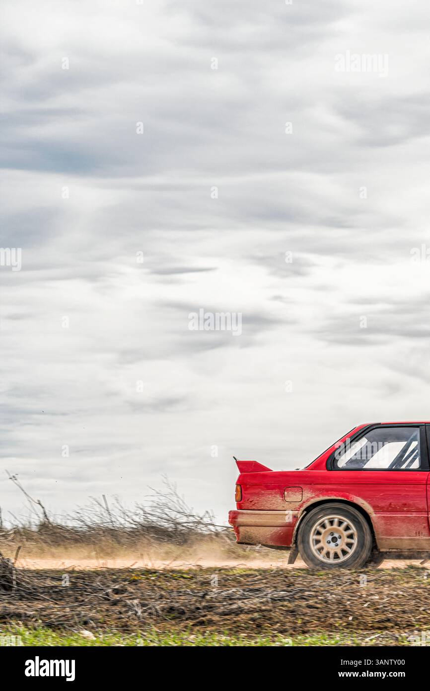Rear view of a red rally car in action on a dirt road with cloudy skies ...