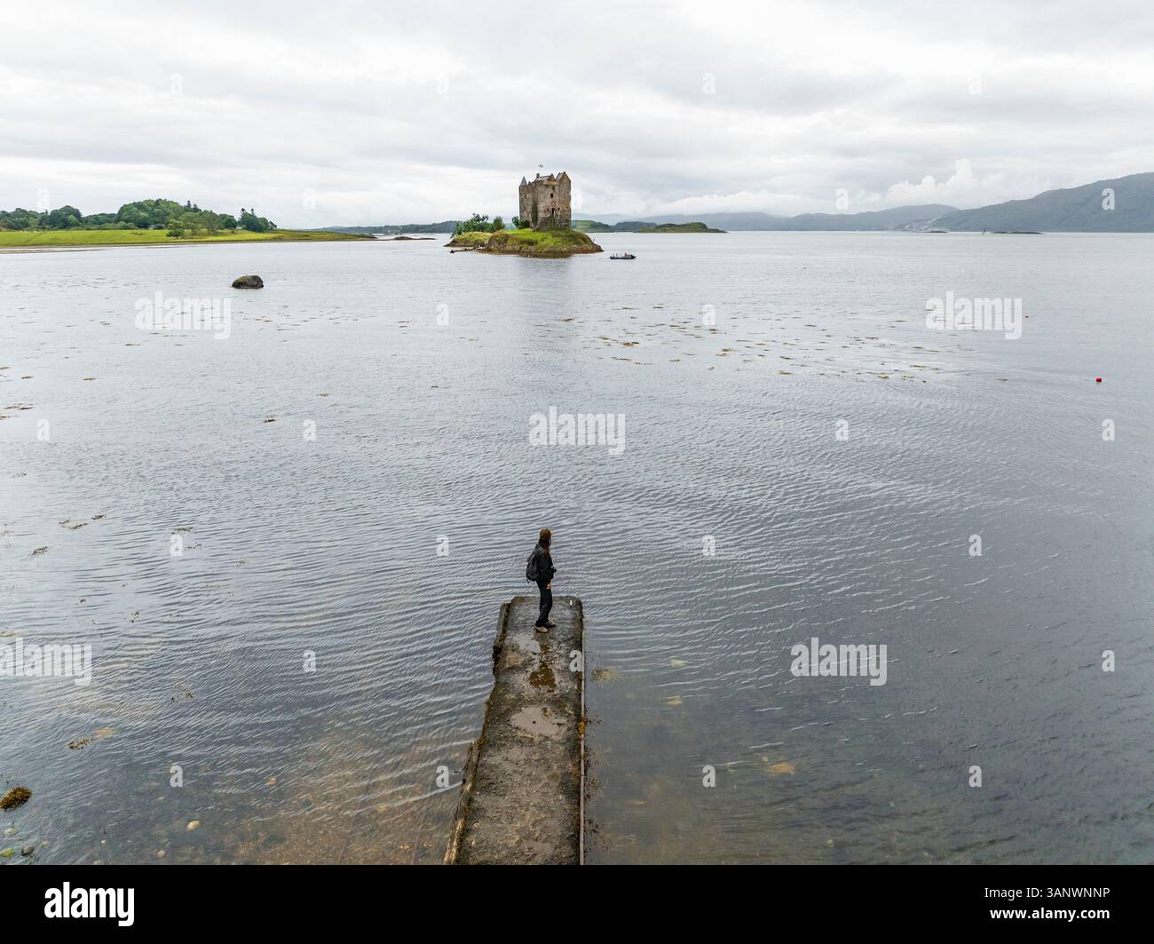 Aerial view of Castle Stalker on Loch Linnhe with a serene woman nearby ...