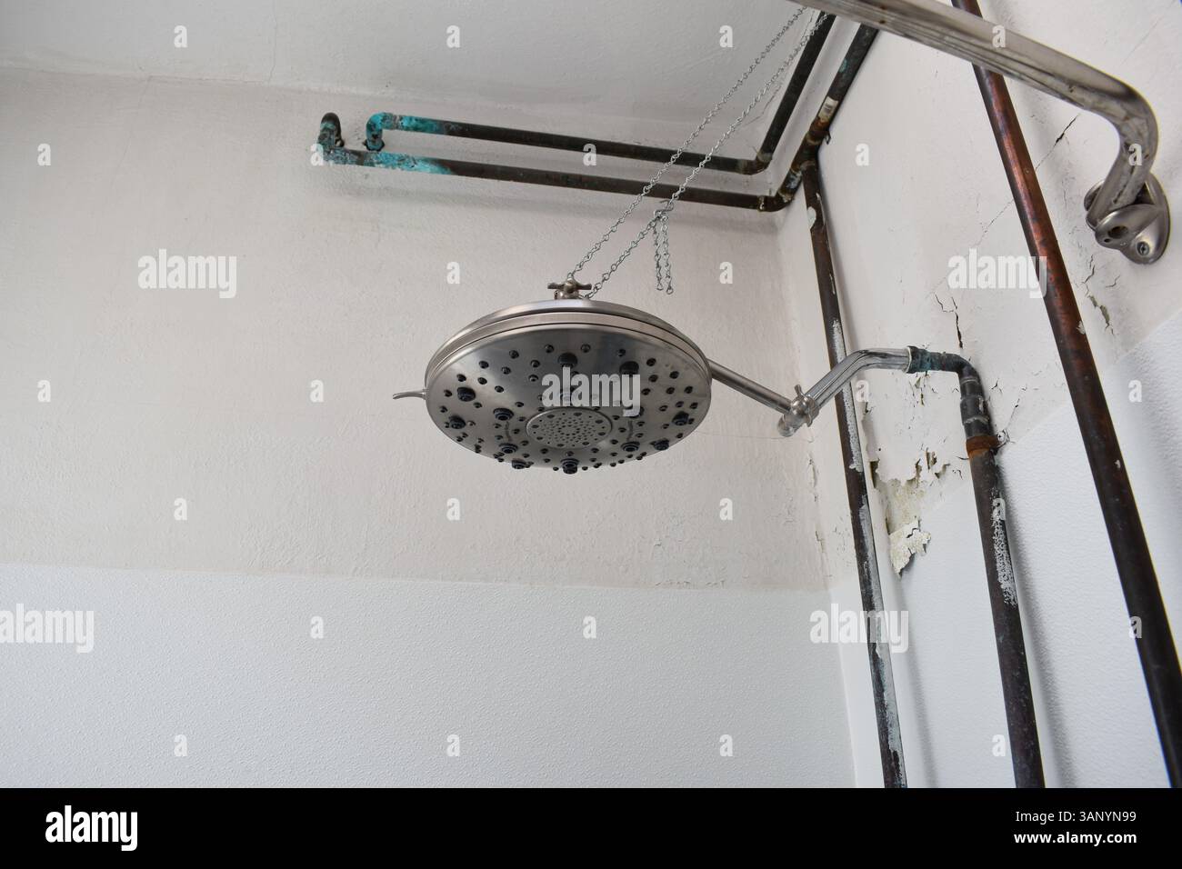 A rustic, outdated shower head fixed to a cracked and peeling wall ...