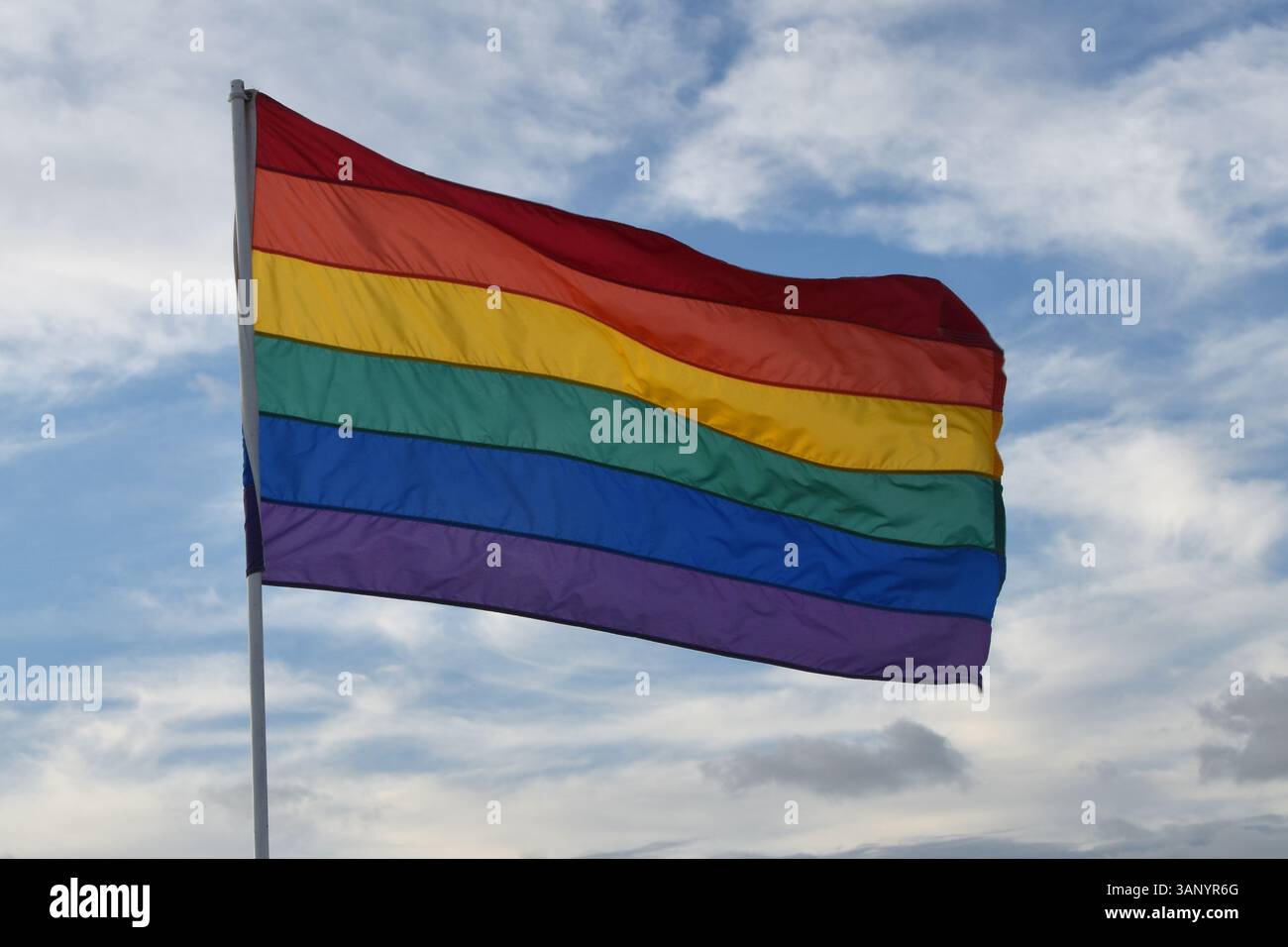 Vibrant rainbow pride flag fluttering in the breeze under a clear blue ...
