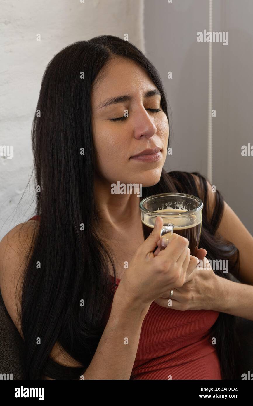 With closed eyes and calm posture, the woman holds her cup in stillness ...