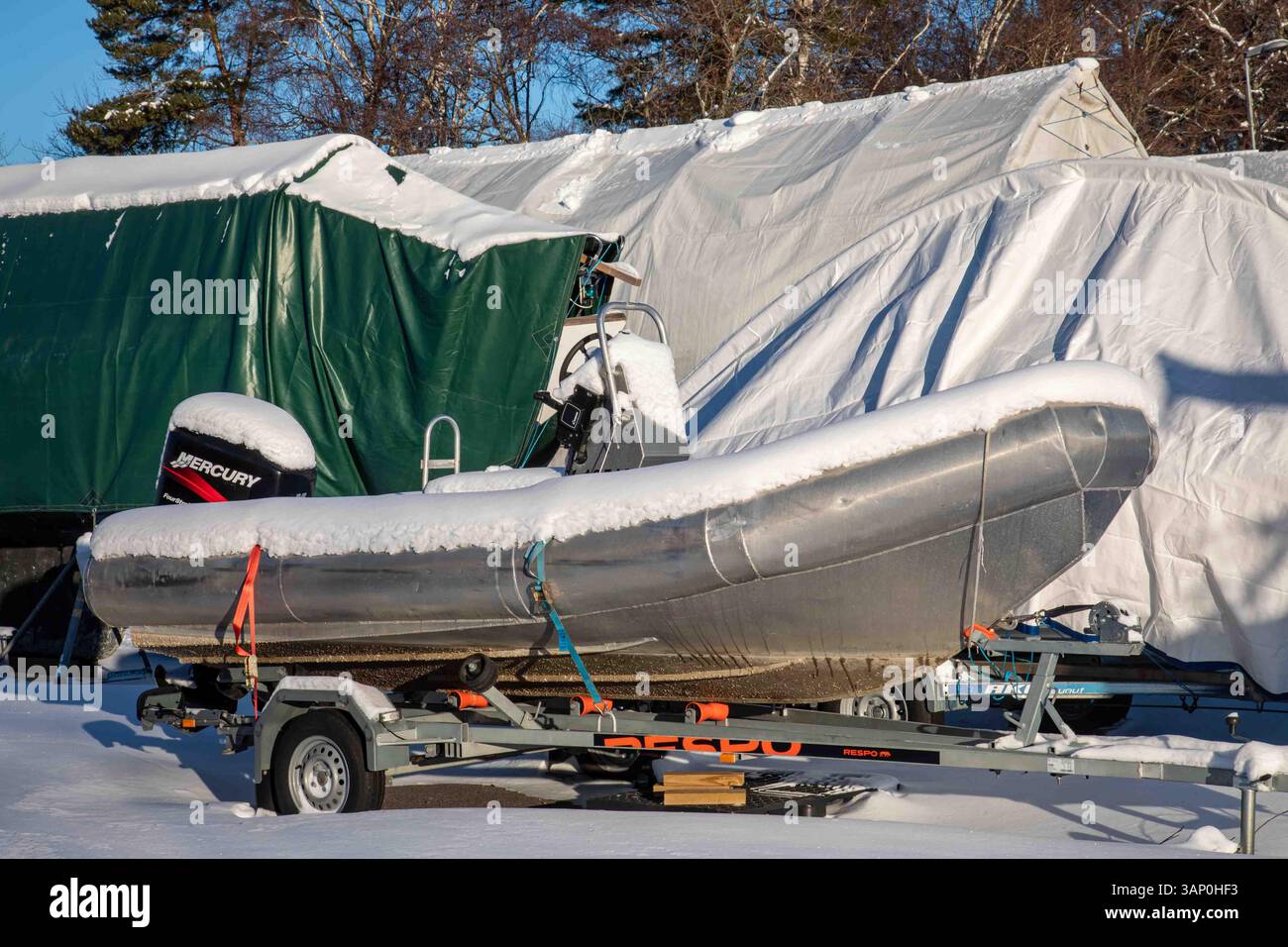 Snow covered aluminum boat with outboard engine on a trailer at ...