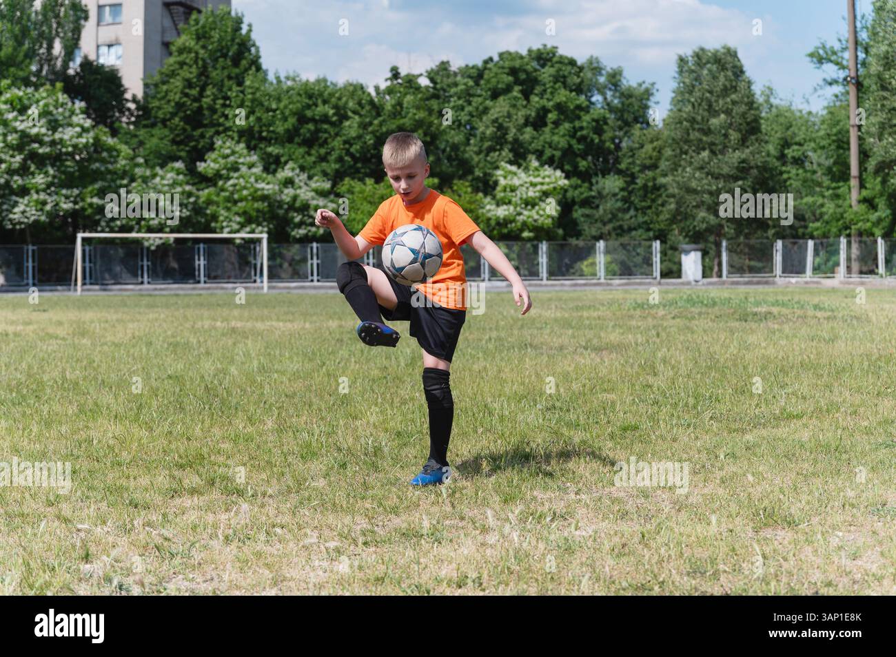 Boy in orange shirt performing kick-ups with a soccer ball on a sunny ...