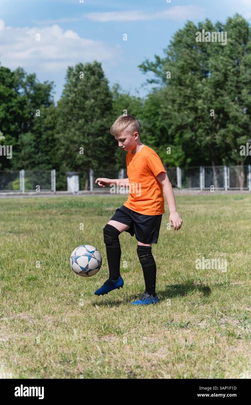 Boy in orange shirt performing kick-ups with a soccer ball on a sunny ...