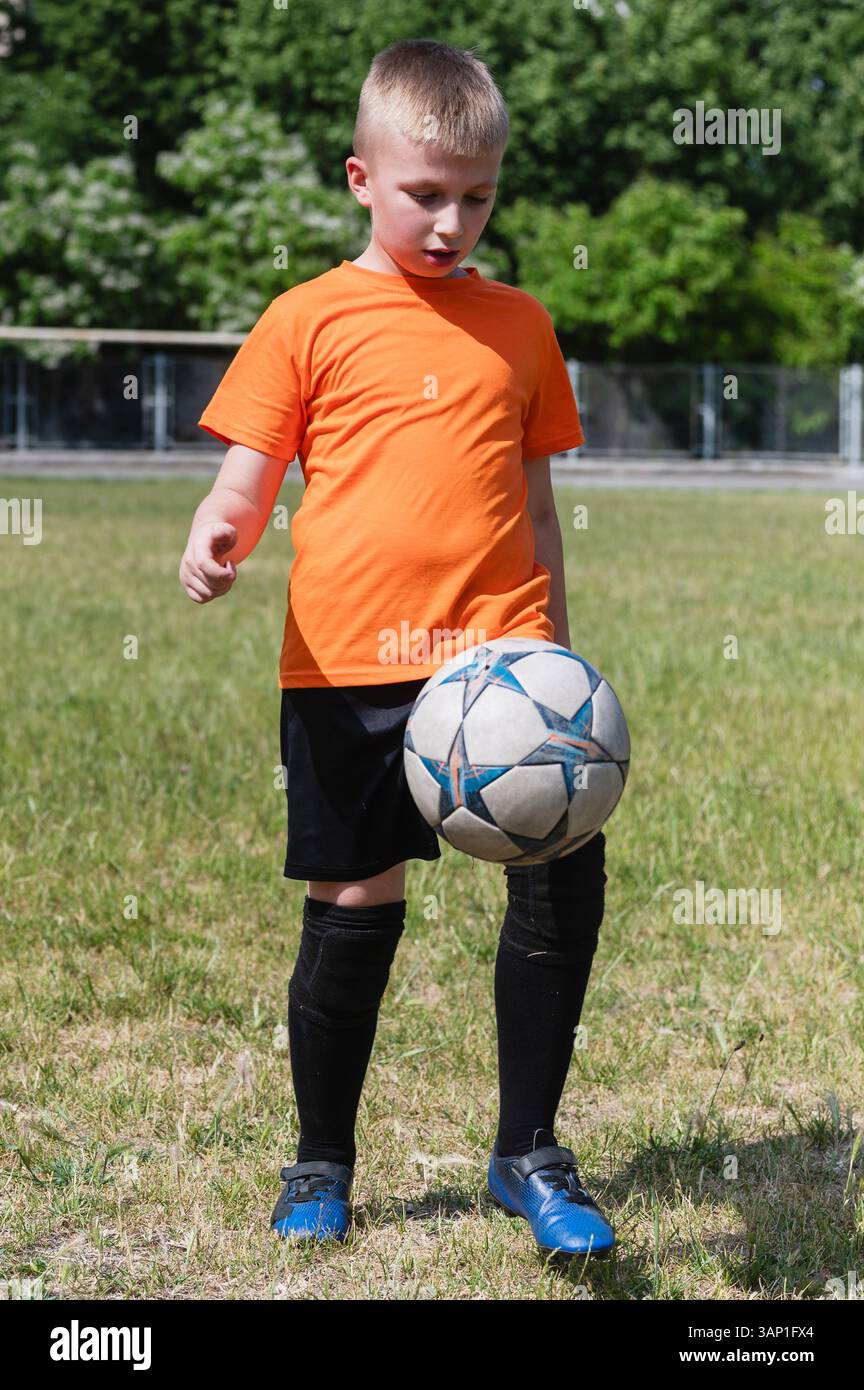 Boy in orange shirt performing kick-ups with a soccer ball on a sunny ...